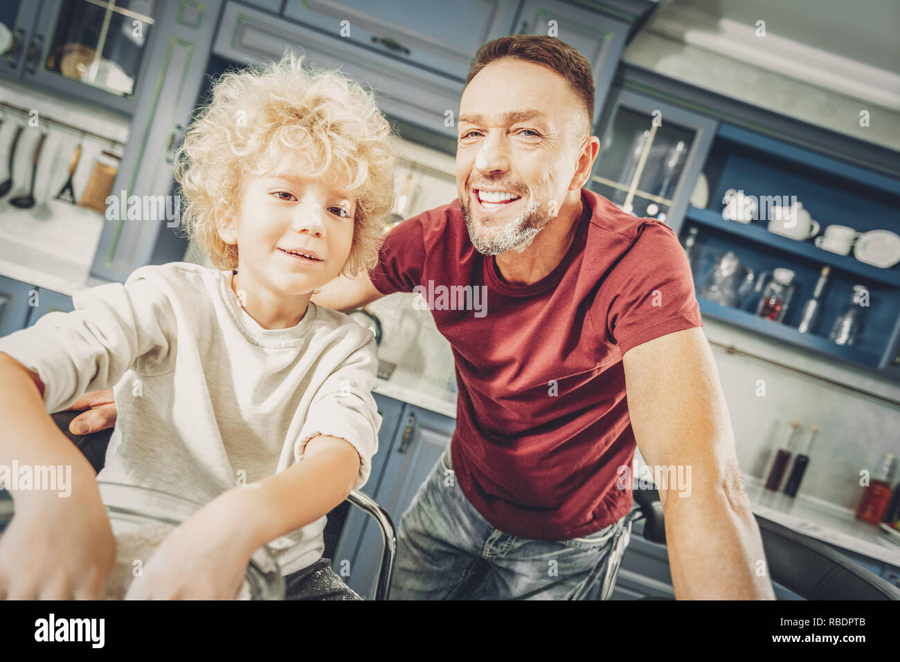 Family culinary. Low angle of adorable positive boy making dough and ...
