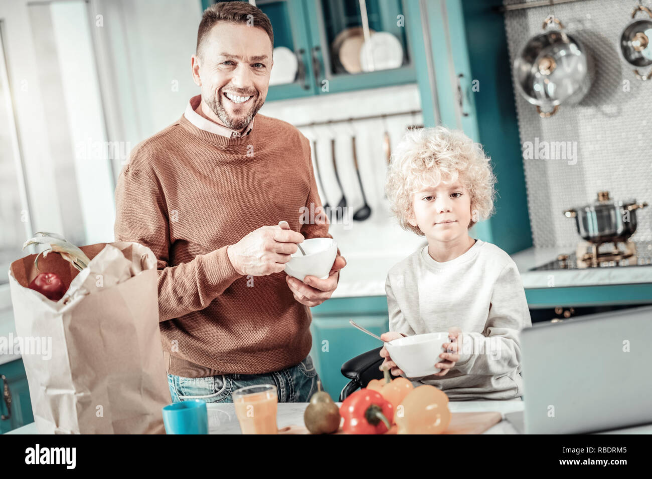 Tasty dinner. Positive father and his son standing in the kitchen while ...