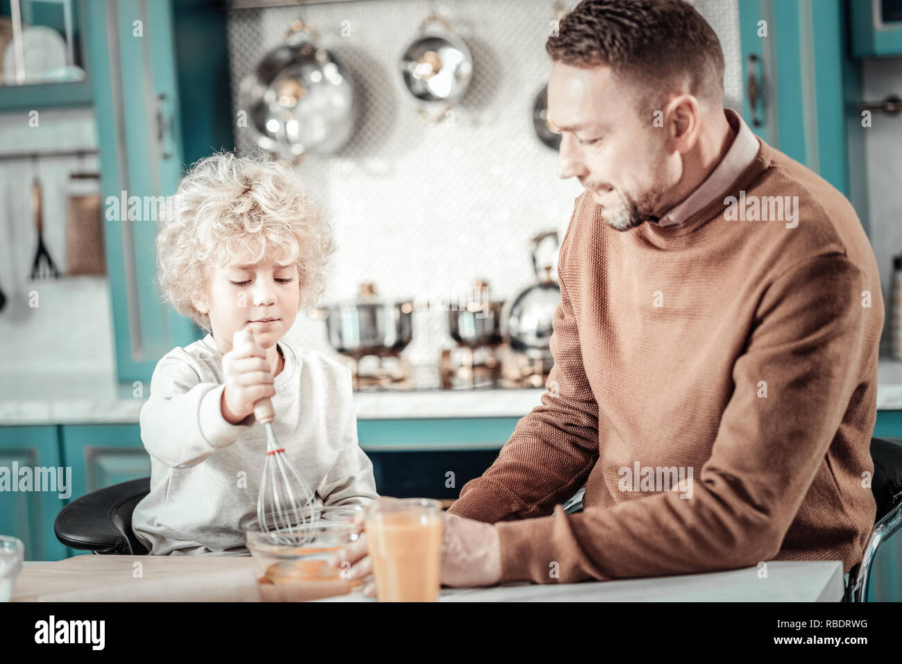 Be careful. Pleased young father leaning elbows on table while holding ...
