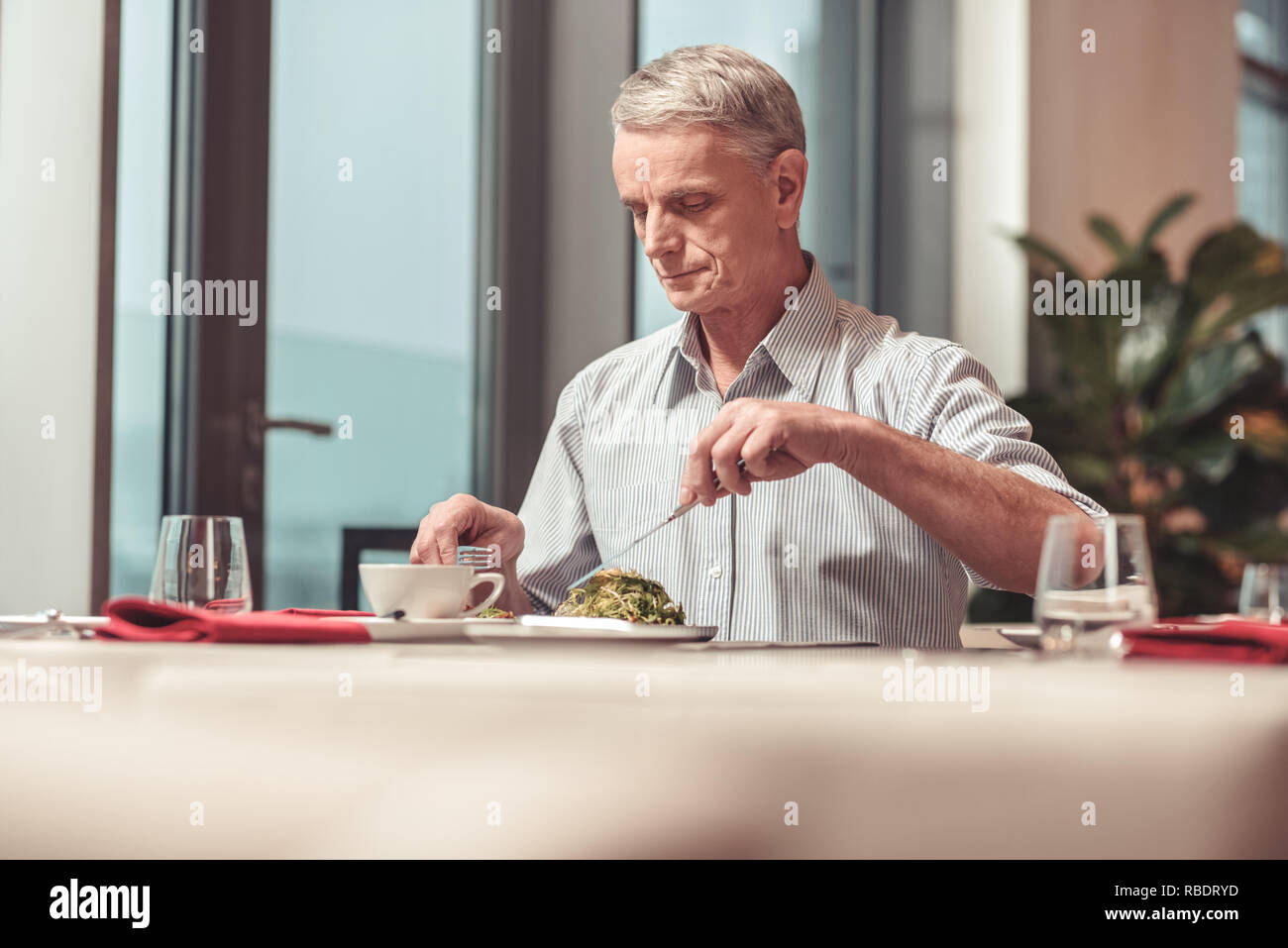 Bad mood. Sad retired man eating a salad while sitting in a restaurant ...