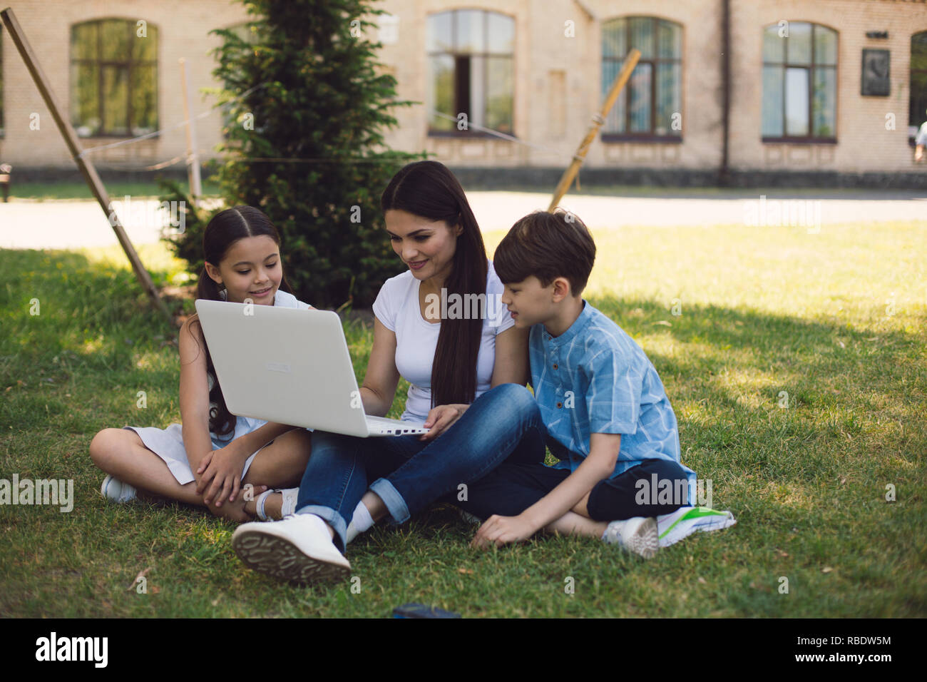 Teacher and two young students use laptop in park Stock Photo - Alamy