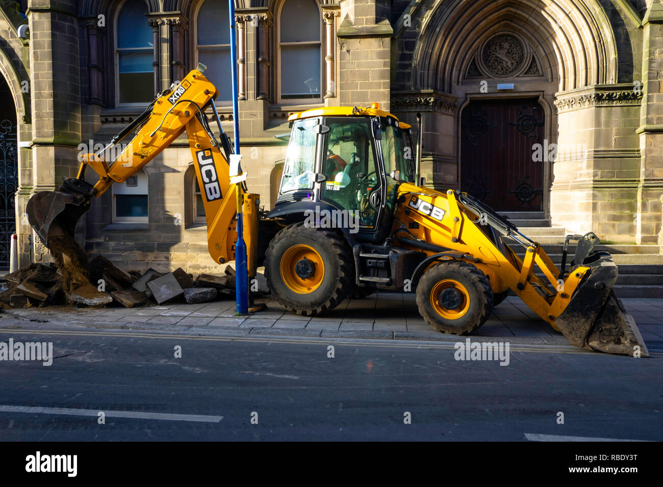 Workman using a JCB excavator removing paving stones on a town centre ...