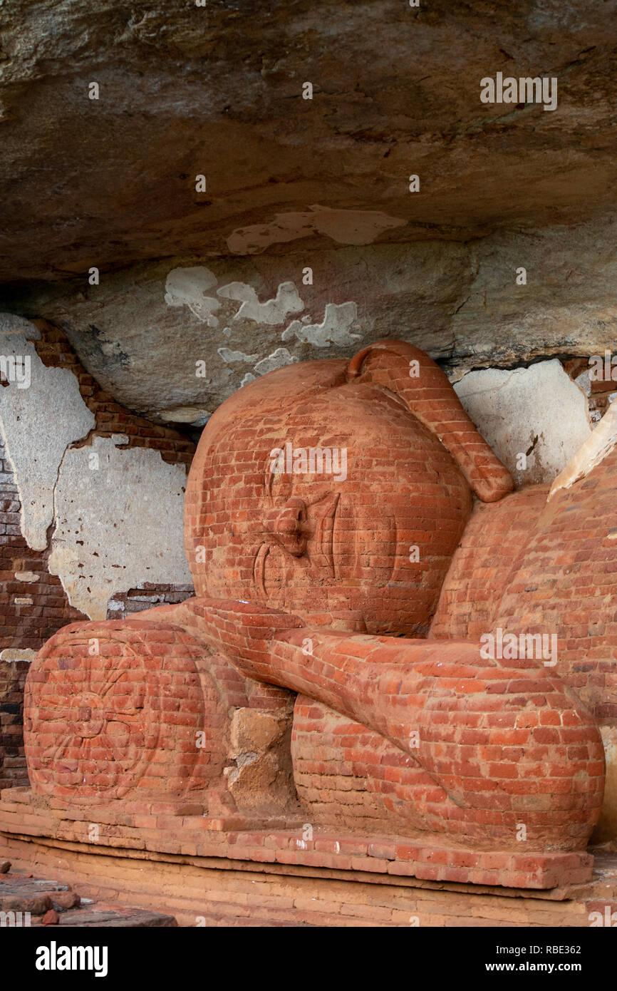 A red brick statue of a Reclining Buddha laid in a hand carved rock ...