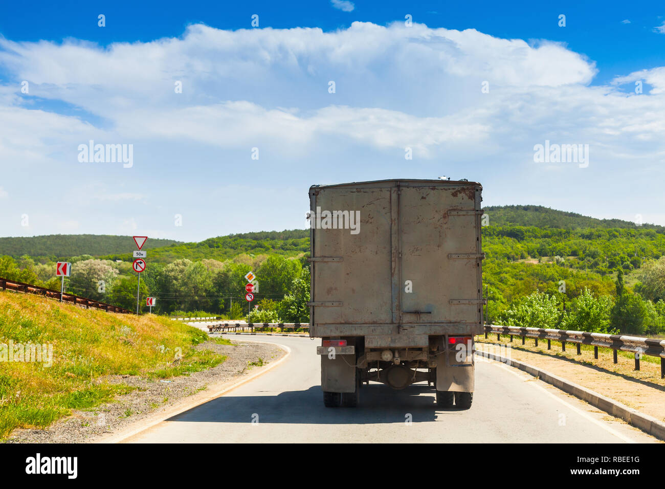 Old truck goes on turning rural road in sunny summer day, rear view ...