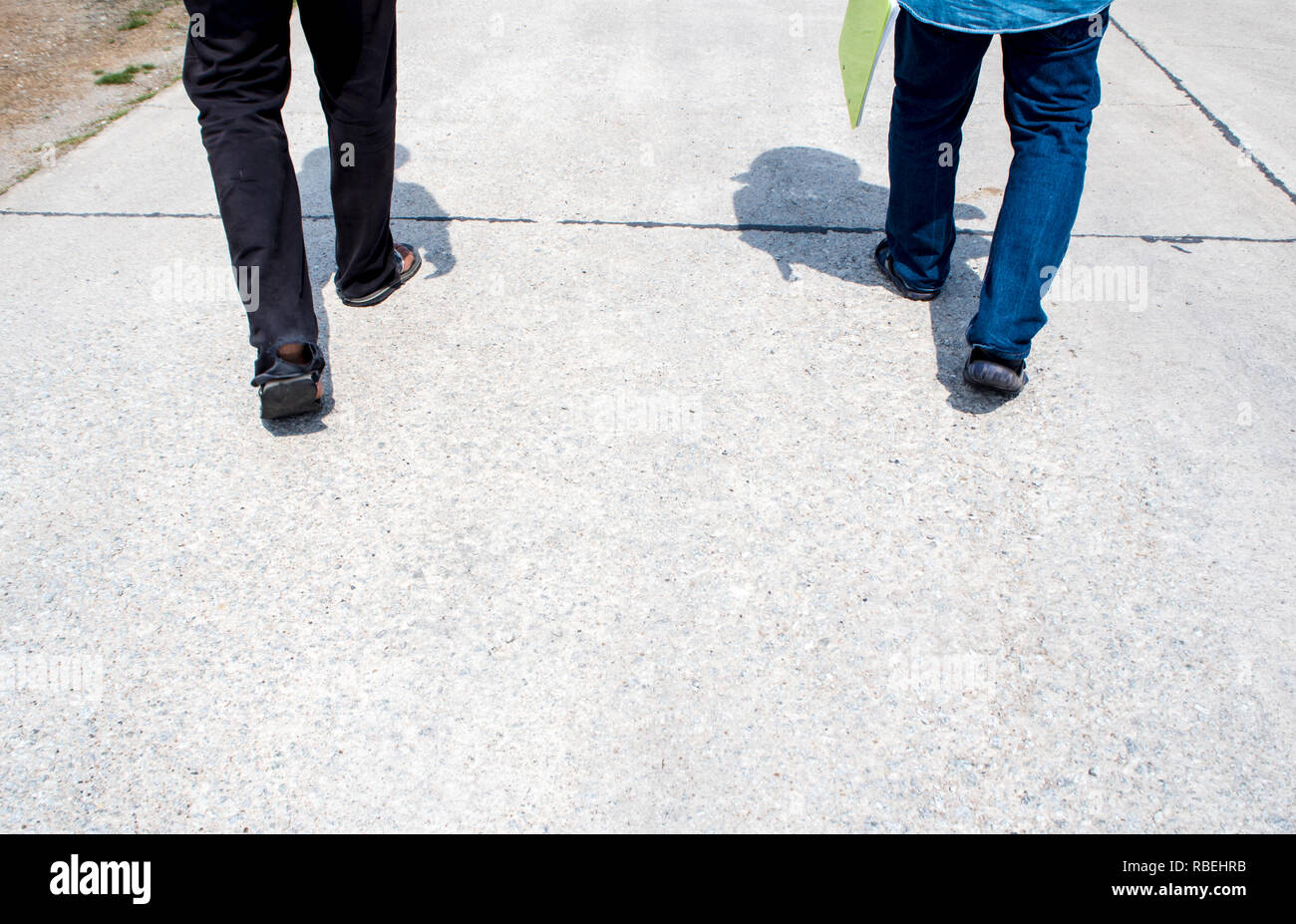 The legs of two men are walking together on a concrete walkway Stock ...