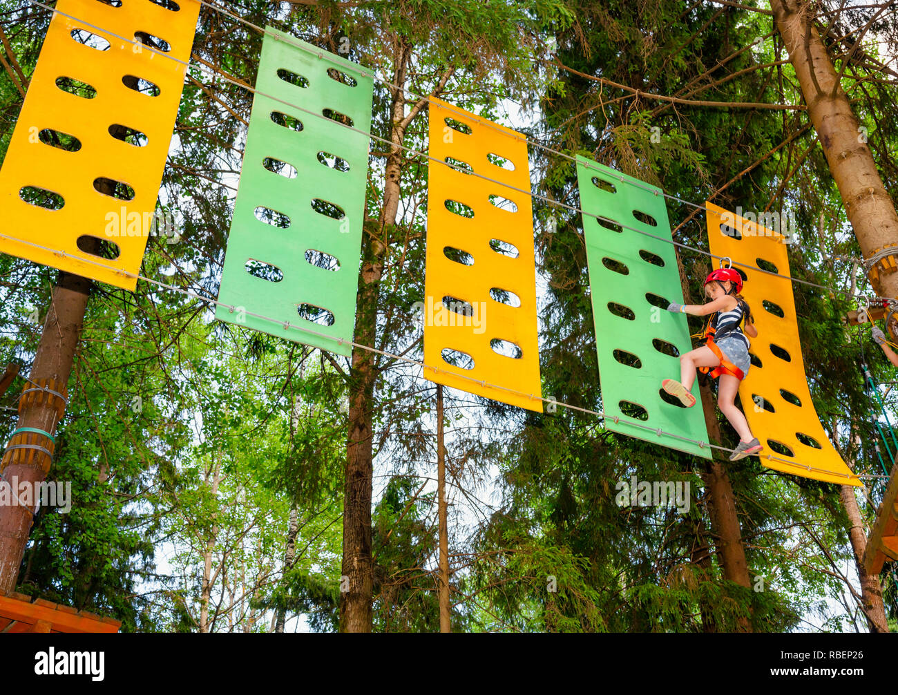 Elementary age girl wearing safety harness passing rope bridge obstacle ...