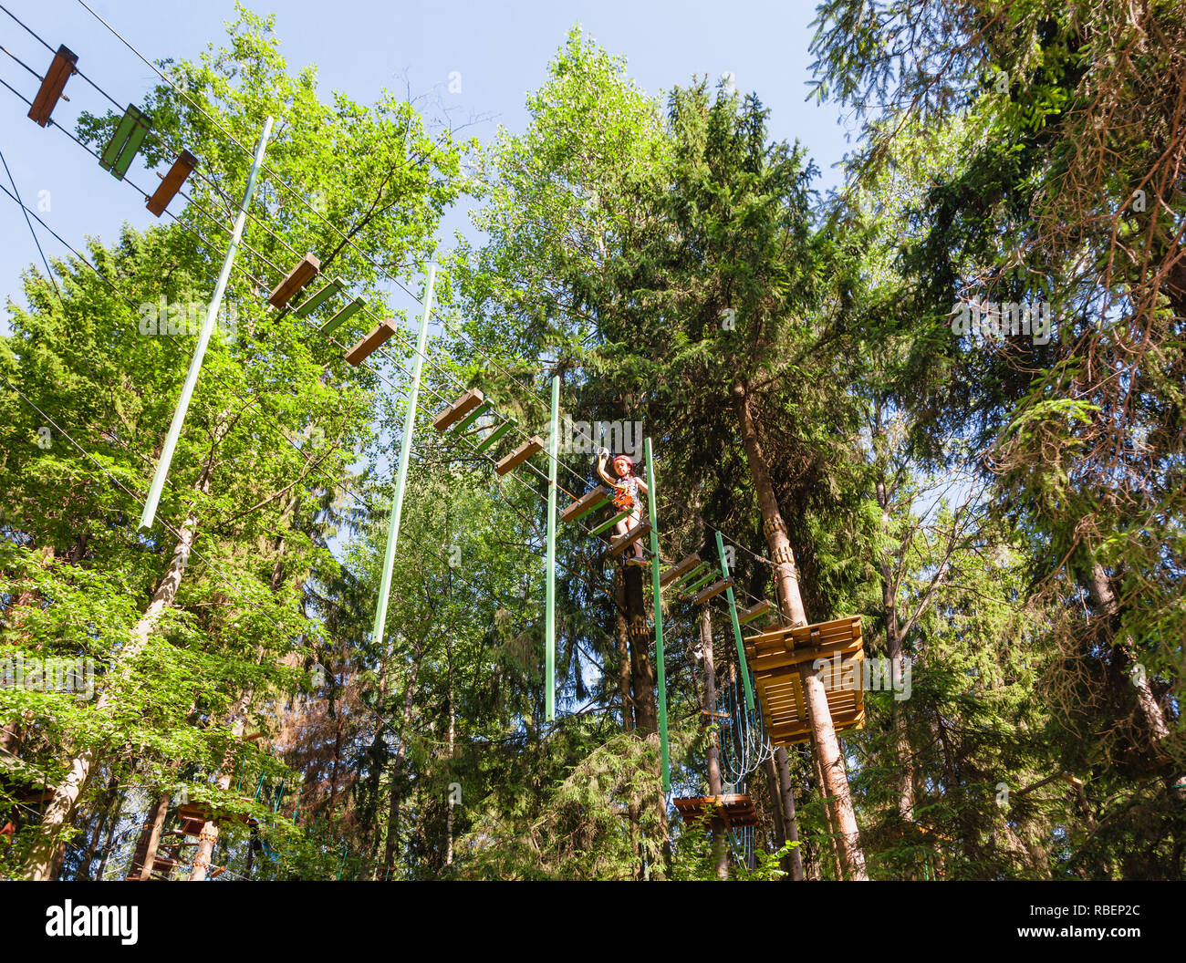 Elementary age girl wearing safety harness passing unstable rope bridge ...
