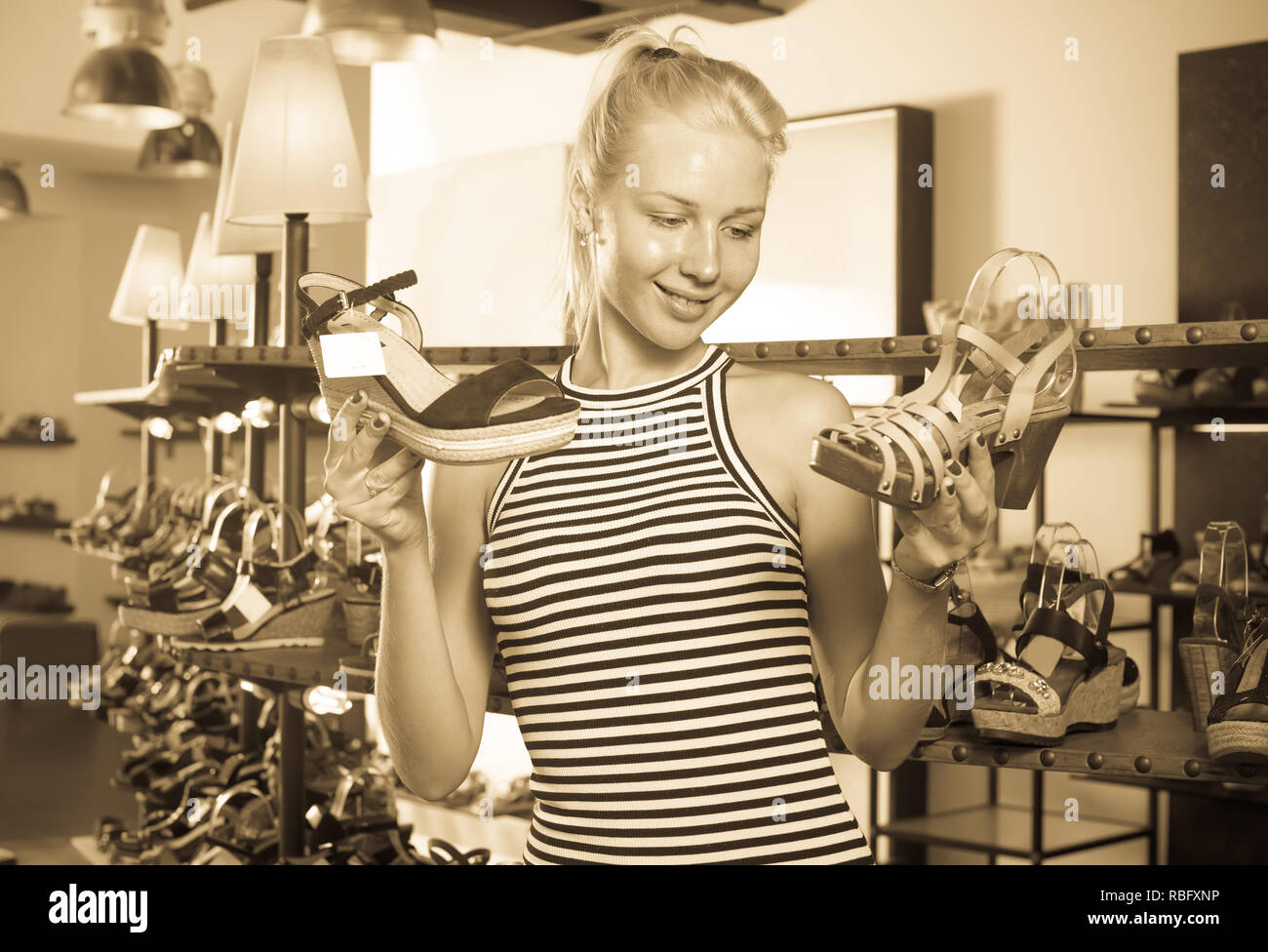 Cheerful woman choosing and comparing two pairs of new shoes in shop ...