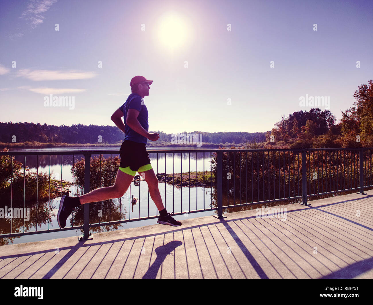 Side shot of healthy middle age man running on lake promenade in sunny ...