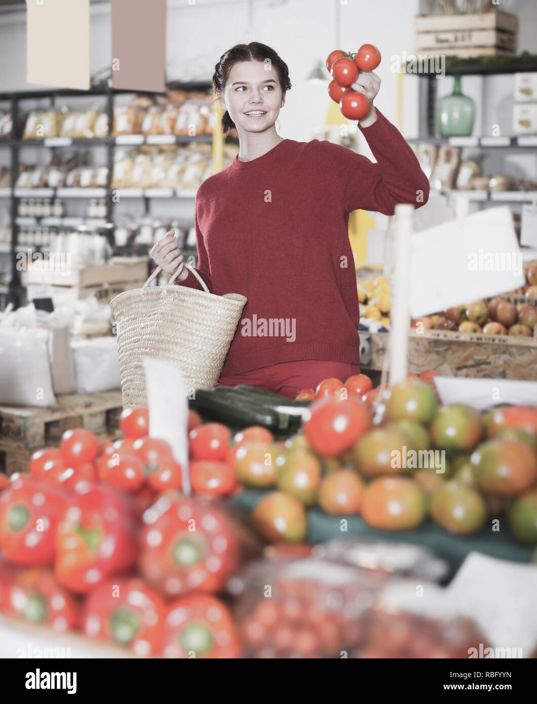 Portrait of happy young female customer selecting tomatoes in grocery ...