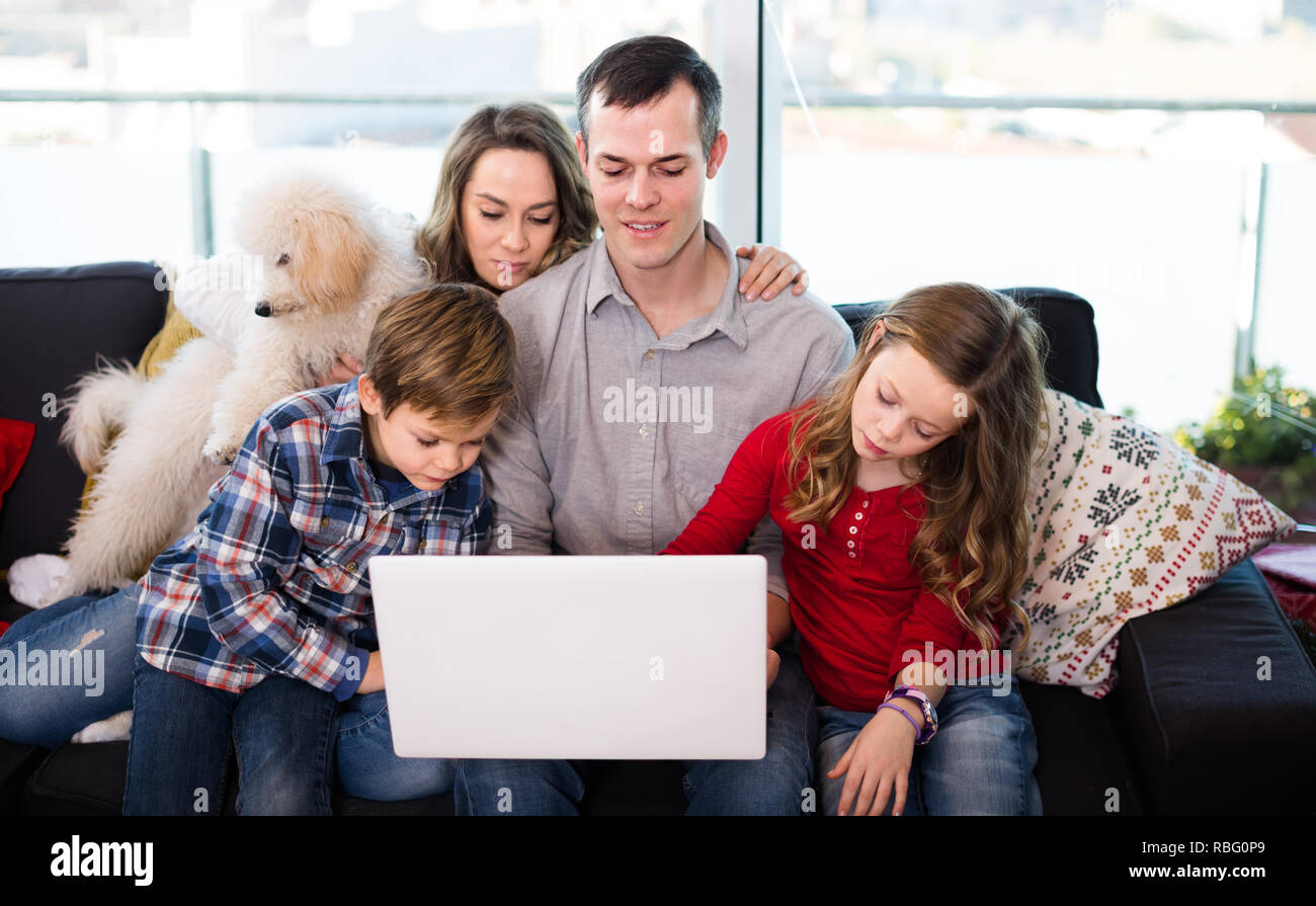 Young family watching movie on laptop together at home on the couch ...