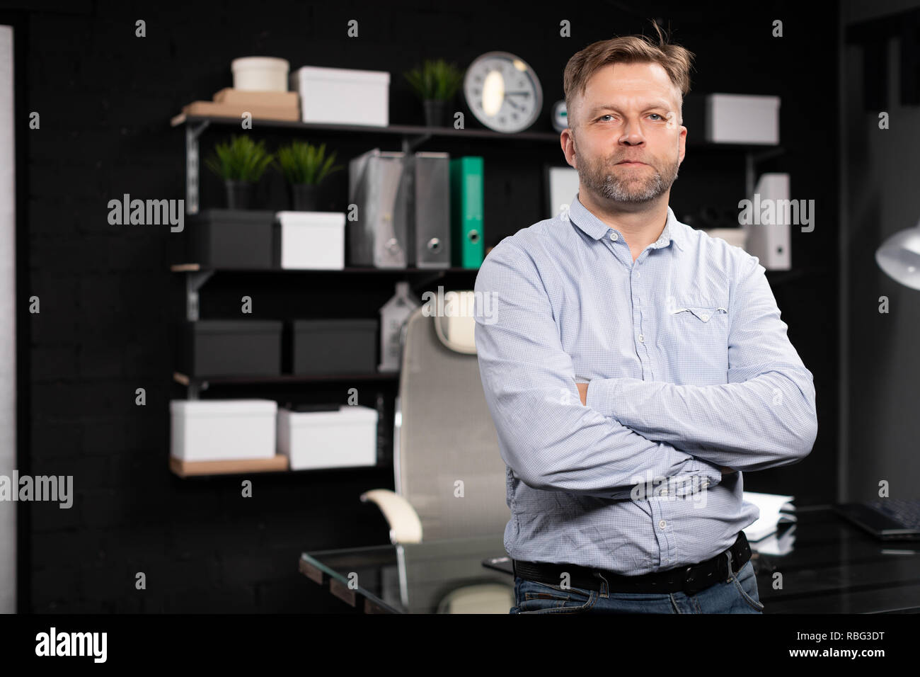 young man stands near the computer table and folded his hands on his ...
