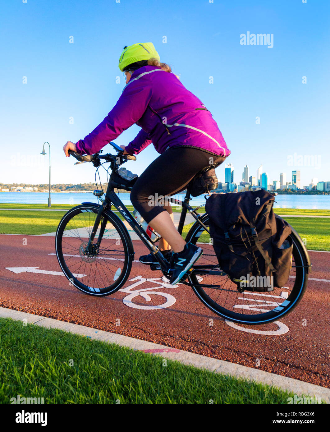 A middle aged woman riding down a bike path / cycle lane with a city ...