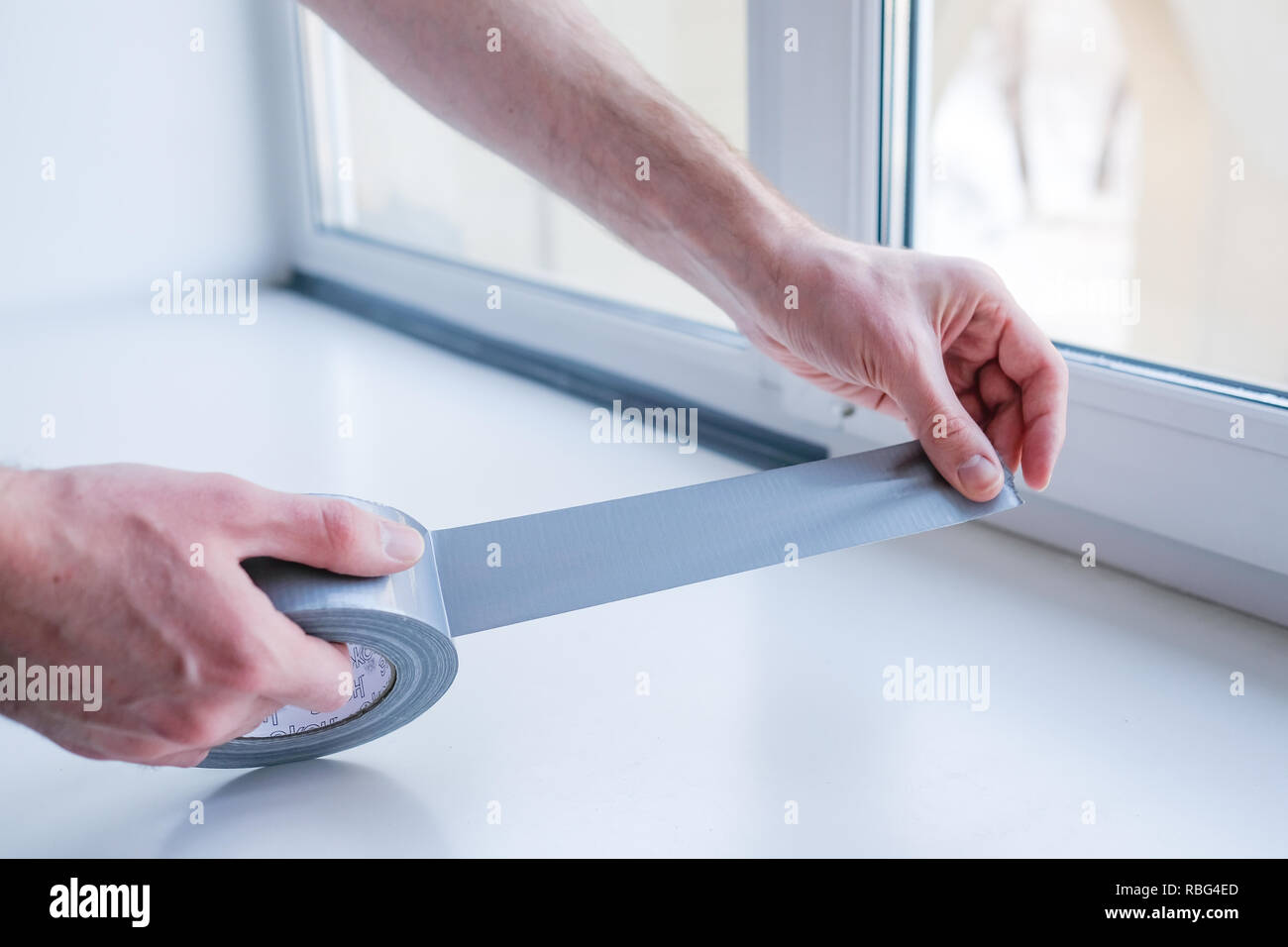 Worker putting sealing gray tape on window in house Stock Photo - Alamy