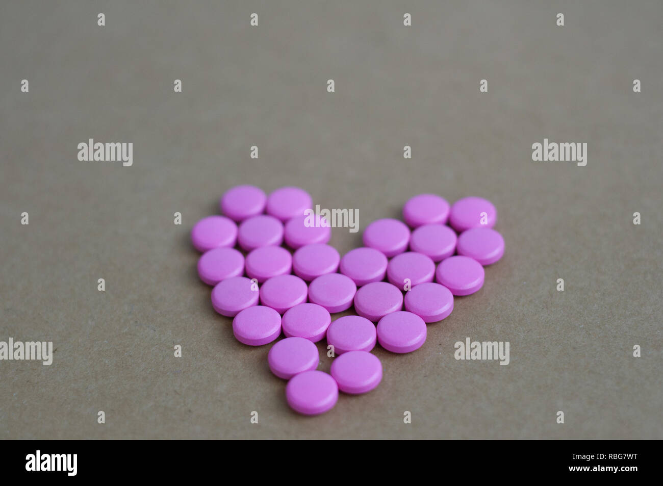 pink pills laid out in shape of a heart on brown background. coloured ...
