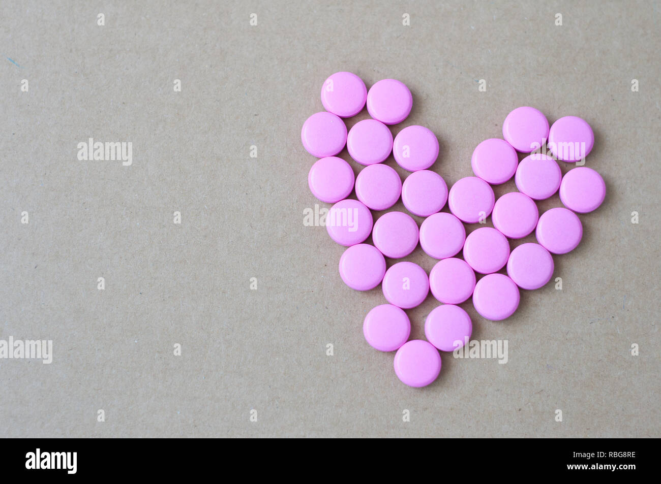 pink pills laid out in shape of a heart on brown background. coloured ...