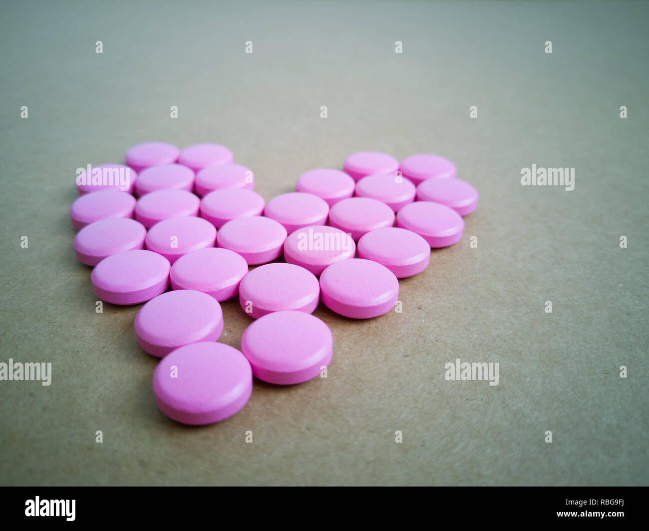pink pills laid out in shape of a heart on brown background. coloured ...