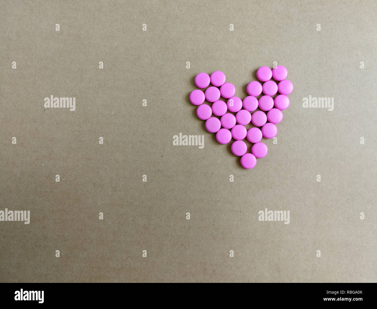 pink pills laid out in shape of a heart on brown background. coloured ...