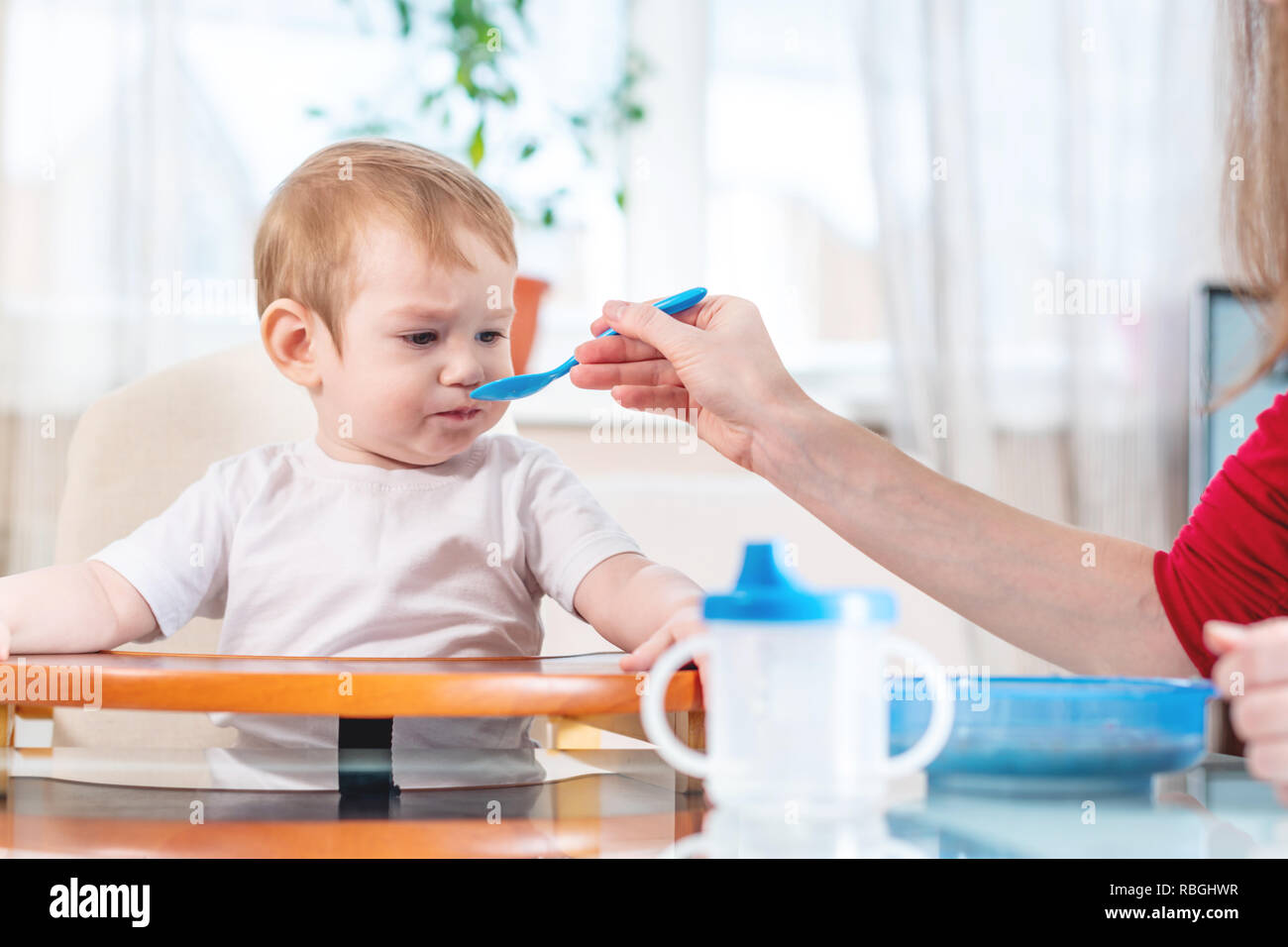 Mother feeding the baby holding out her hand with a spoon of porridge ...