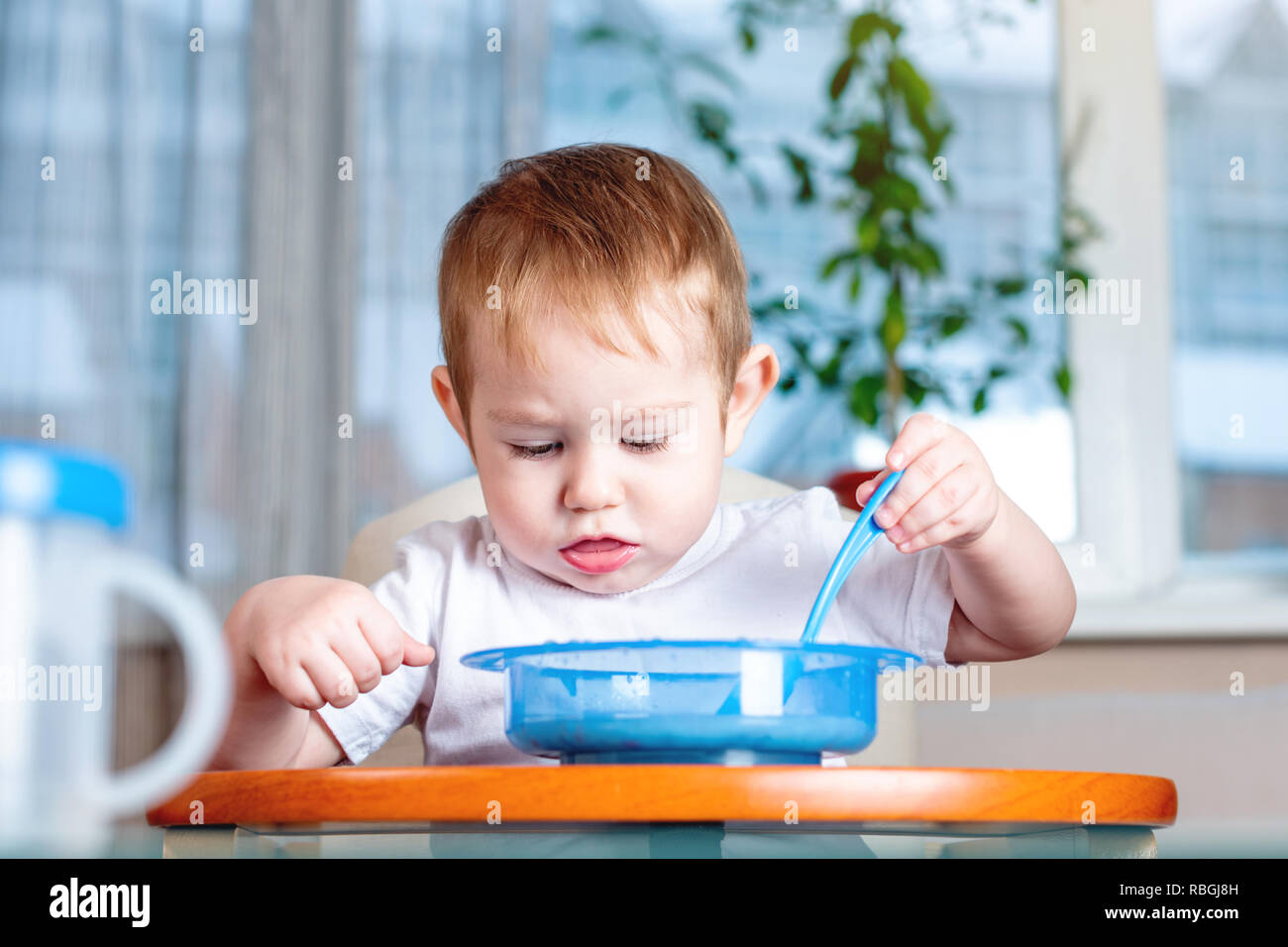 Little baby boy learning to eat with a spoon himself at the kids table ...