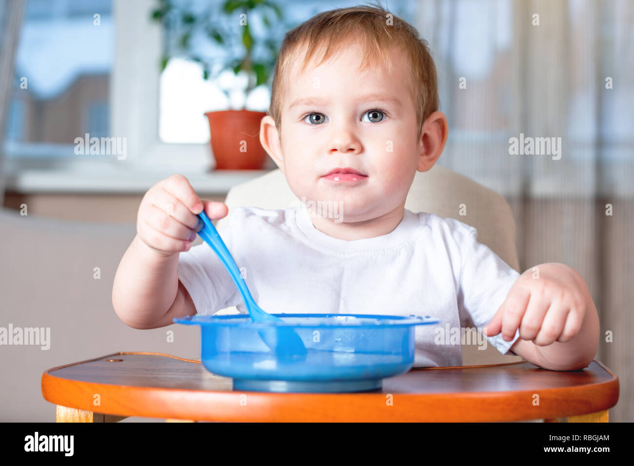 Little baby boy learning to eat with a spoon himself at the kids table ...