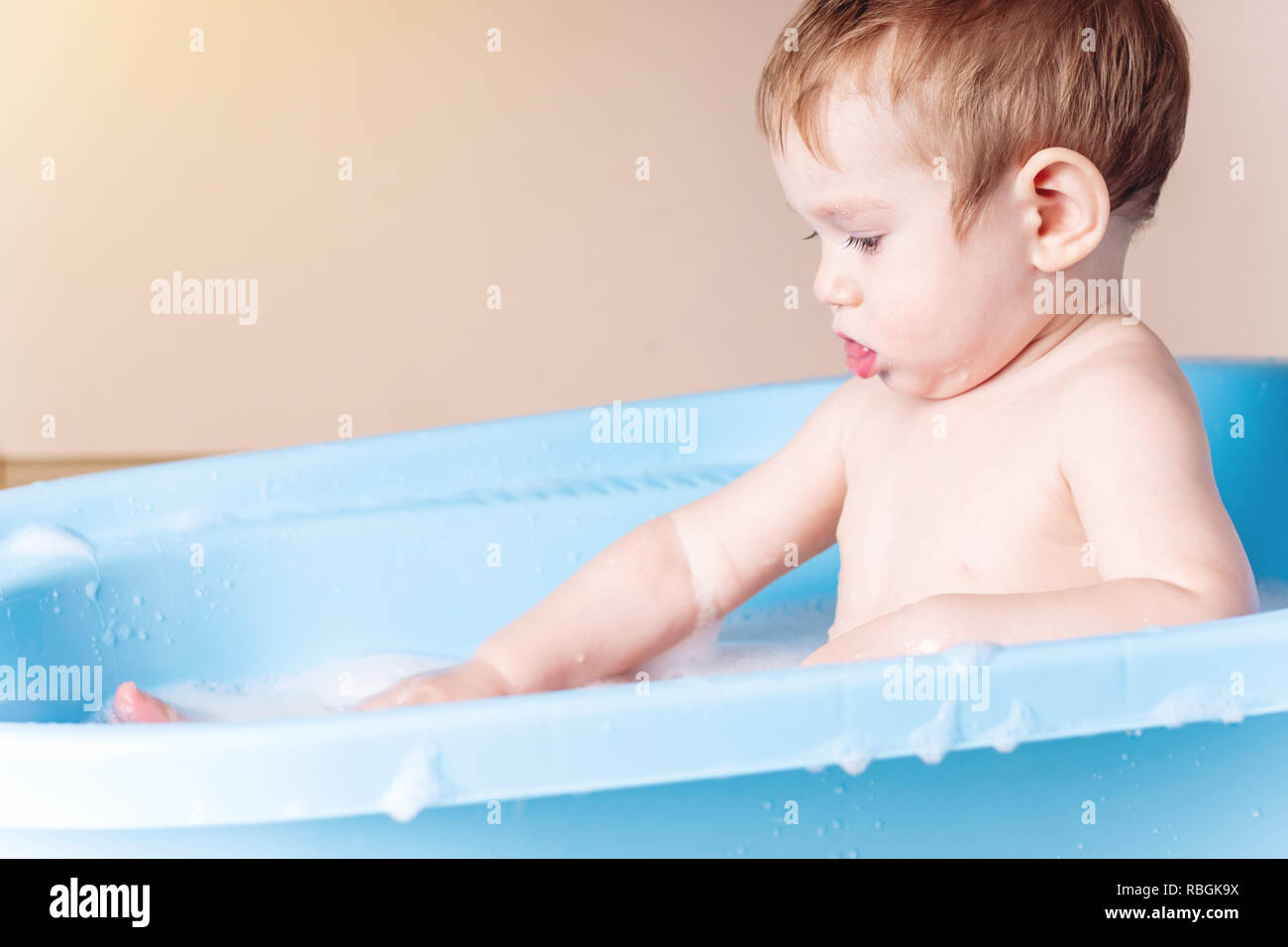 Cute baby washing in blue bath in bathroom. Boy playing with water and ...
