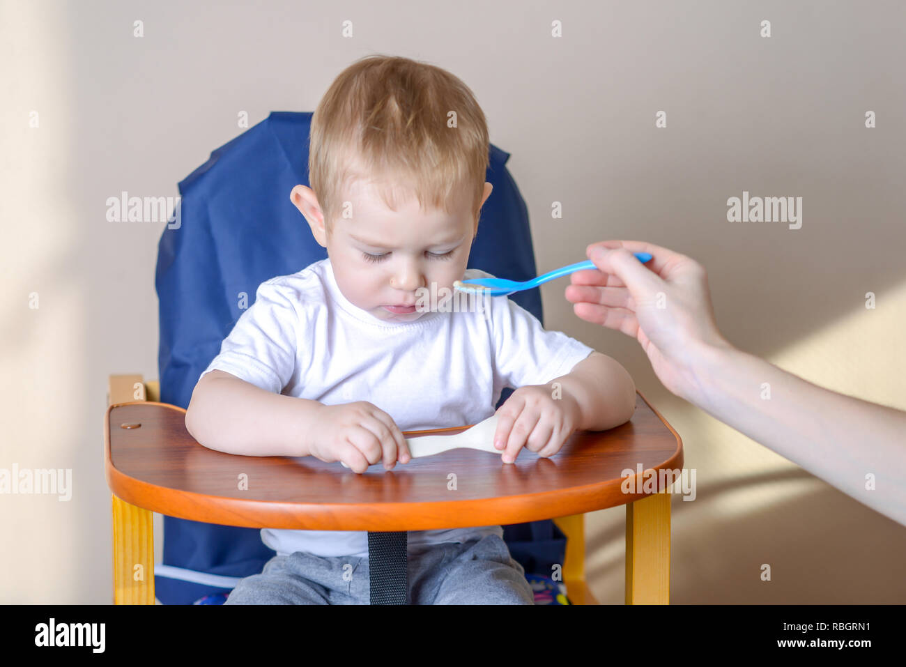 Little child boy learns to eat at the children's table in the kitchen ...