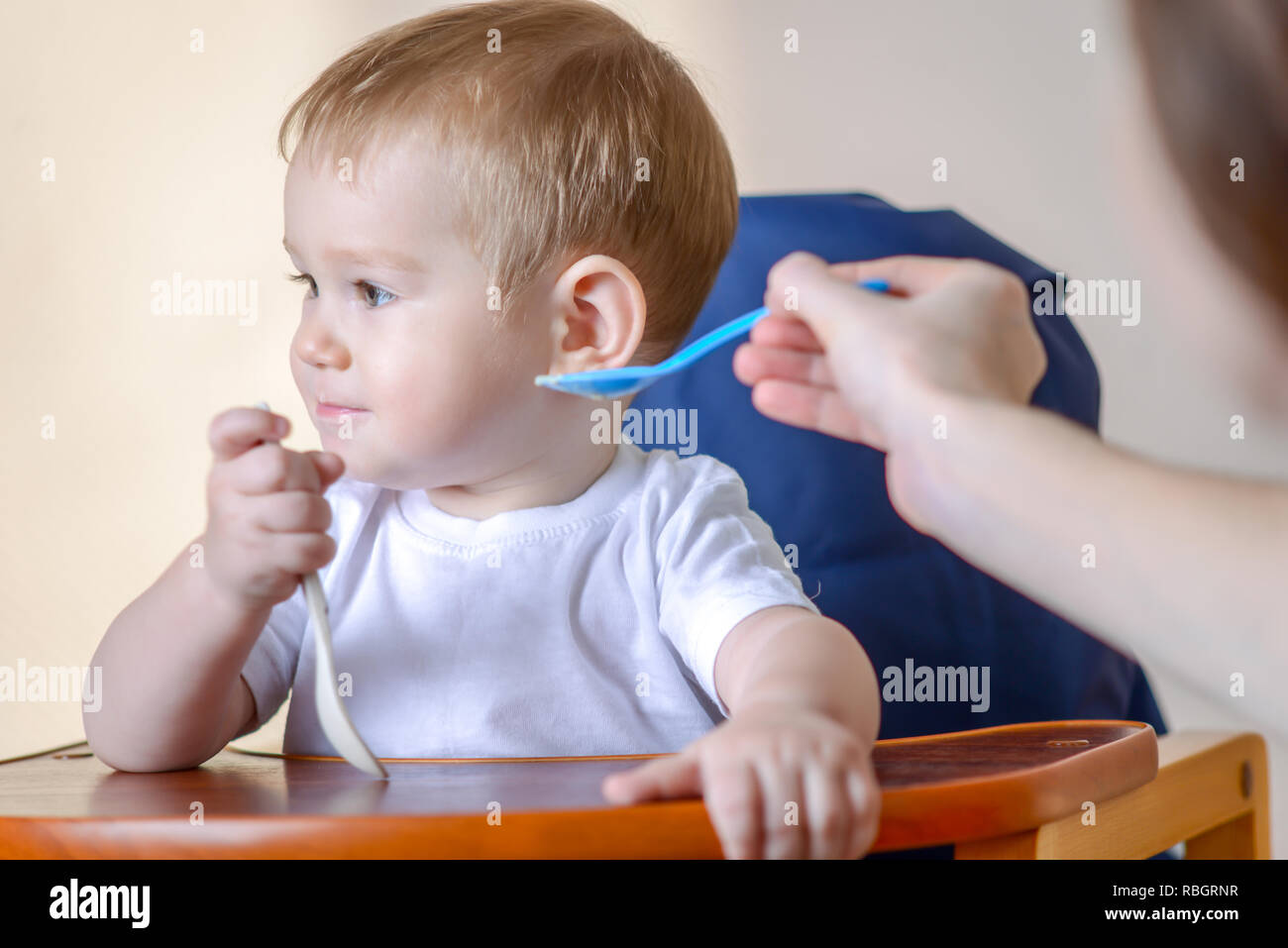 Little child boy learns to eat at the children's table in the kitchen ...