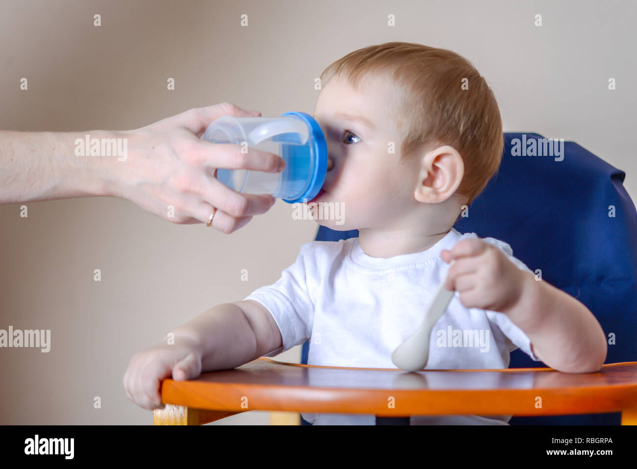 Little baby boy drinking water while sitting on a chair in the kitchen ...