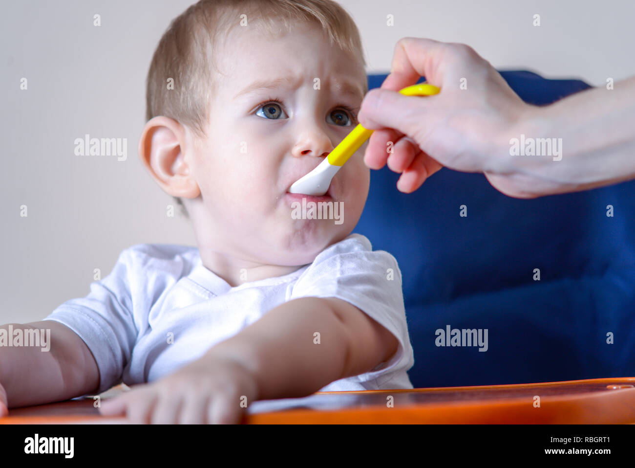 Little child boy learns to eat at the children's table in the kitchen ...