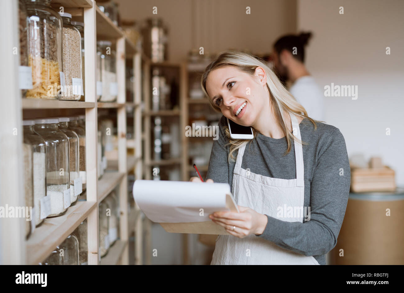 A female shop assistant with smartphone working in a zero-waste shop ...