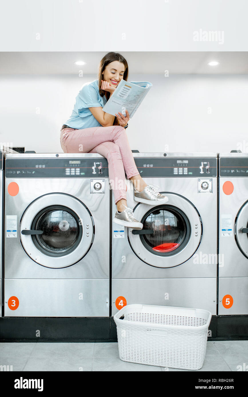 Young woman sitting on the washing machine reading some magazine while ...