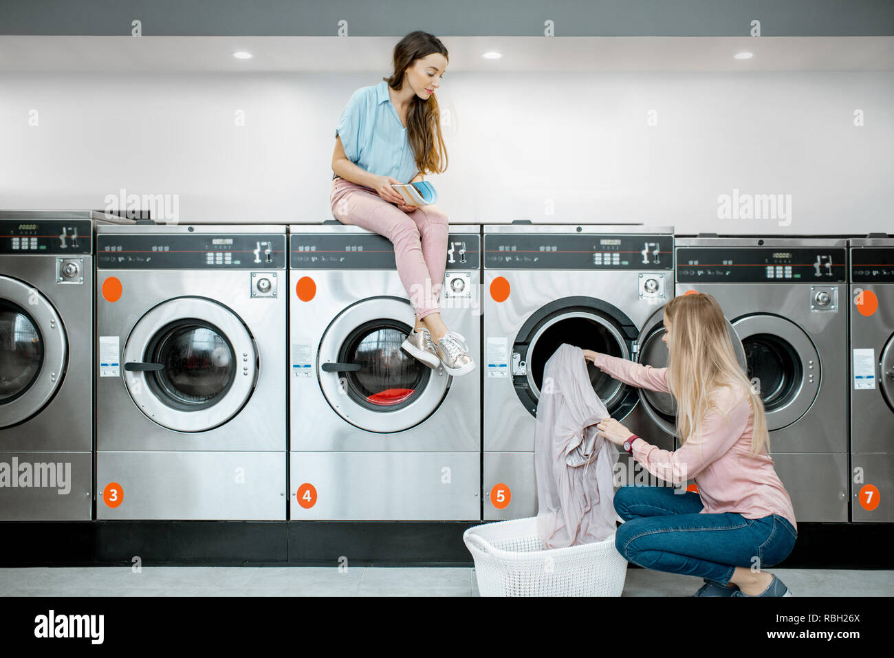 Two cheerful girlfriends preparing for washing loading clothes into the ...