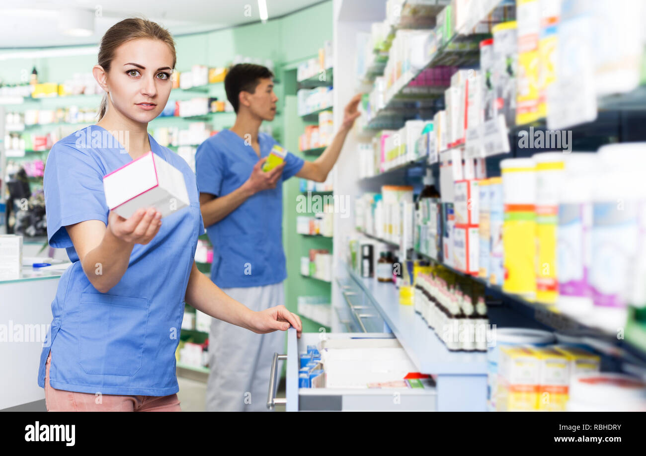 Positive woman specialist is attentively looking medicines in lockers ...