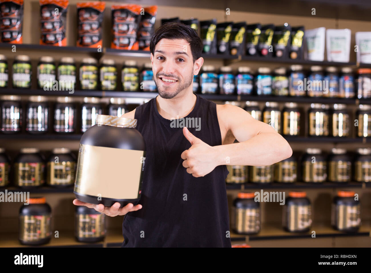 Young bodybuilder holding thumb up and big pot of sport nutrition ...