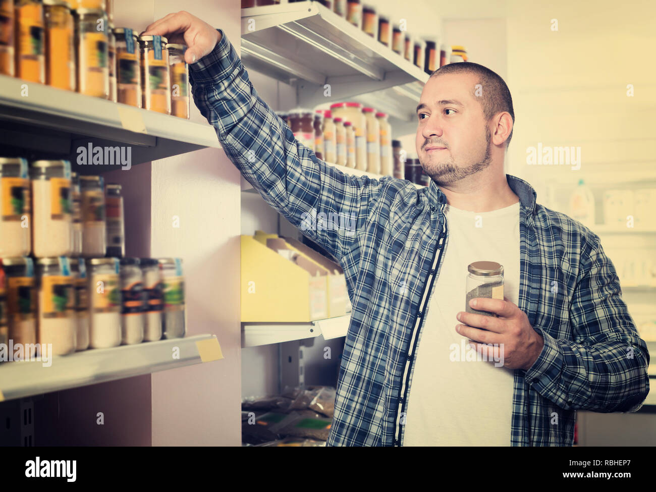 Cheerful male customer choosing pasta of nuts in average food shop ...