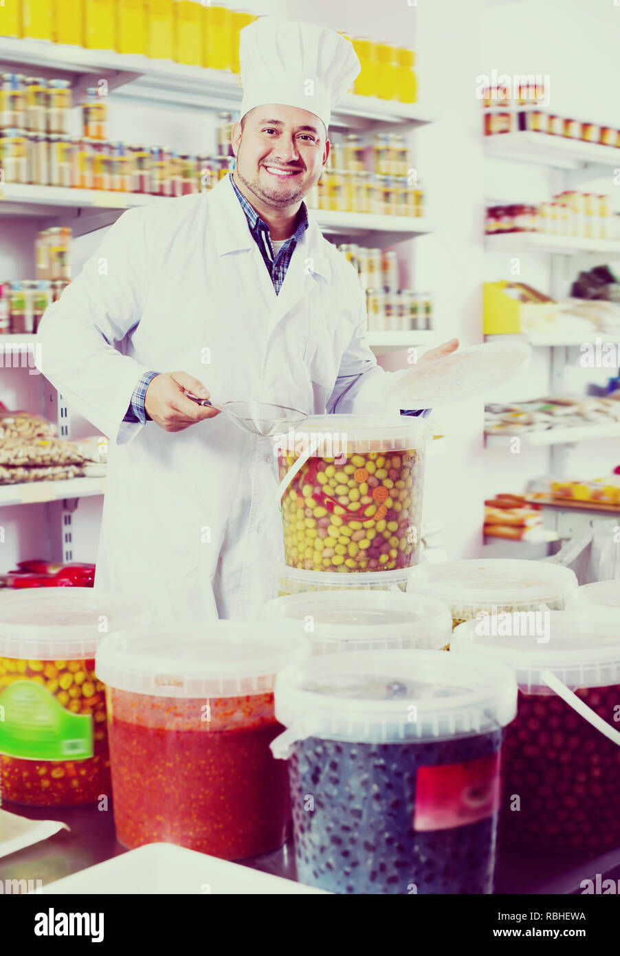 Salesman offering salted olives with filling in ordinary food shop ...