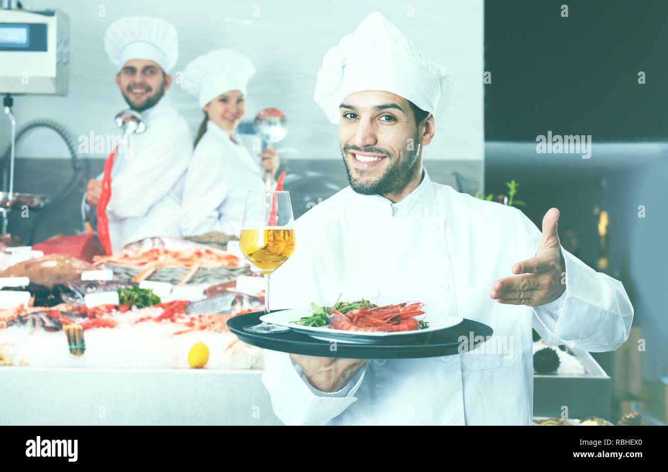 Portrait of positive smiling chef standing with serving tray in fish ...