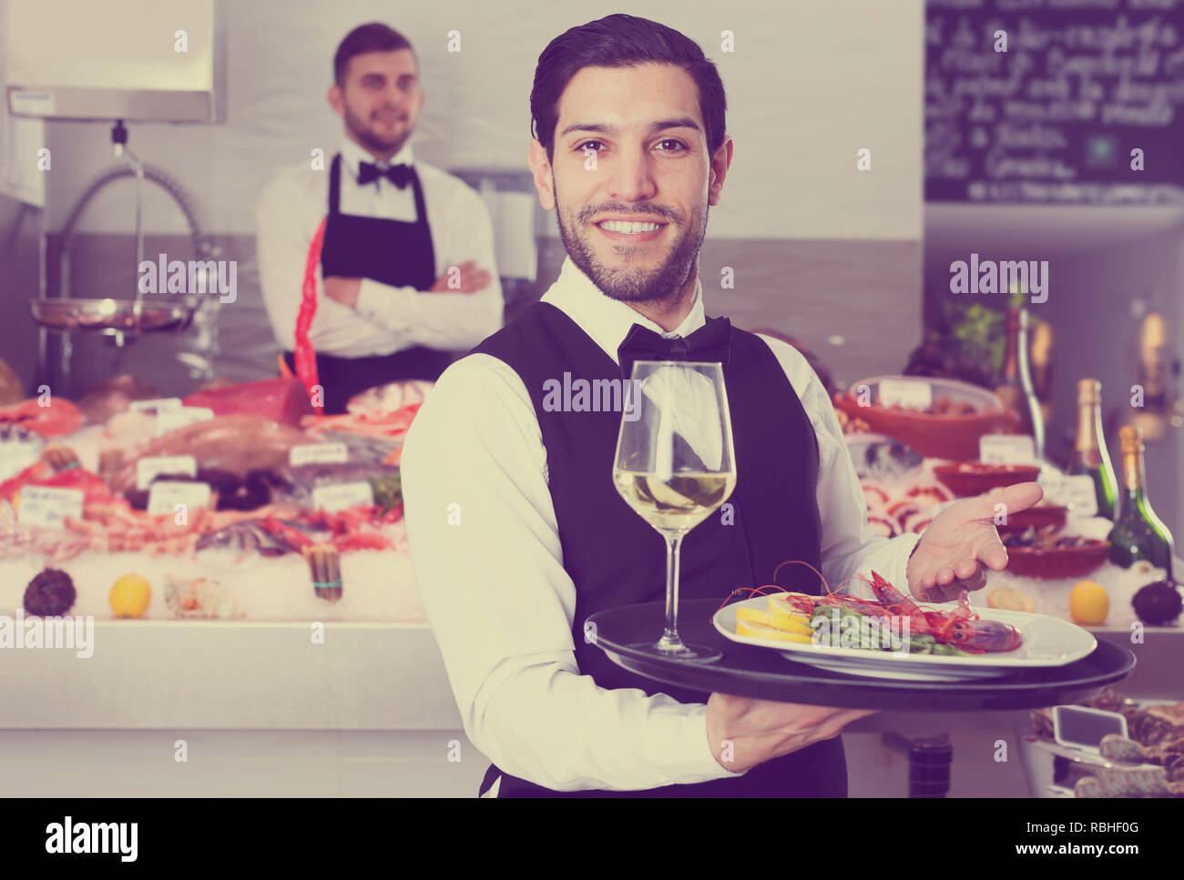 Smiling waiter with serving tray showing dishes in fish restaurant ...