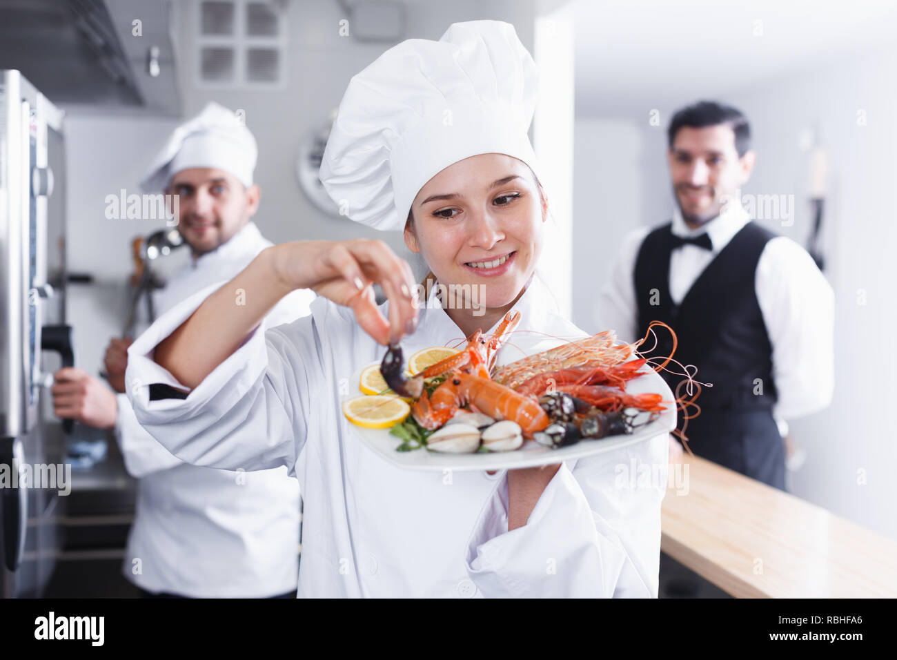 Attractive young woman chef of fish restaurant busy preparing seafood ...