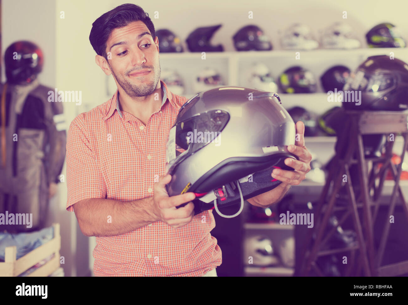 Smiling man is choosing moto helmet for head protection in sport shop ...