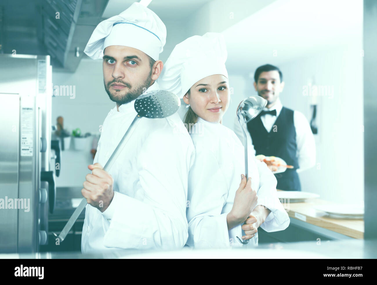 Portrait of two professional cooks in kitchen, restaurant waiter with ...