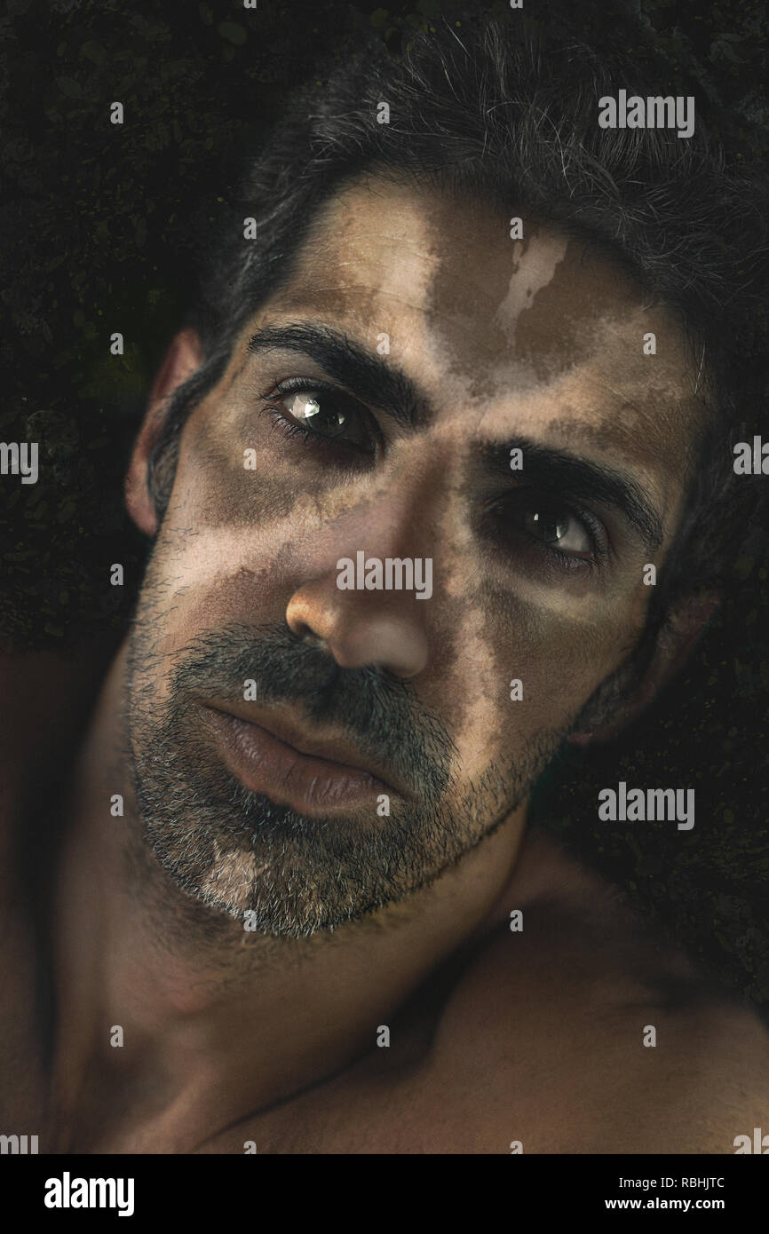 An indigenous man with dark skin and with a clear X makeup on his face ...