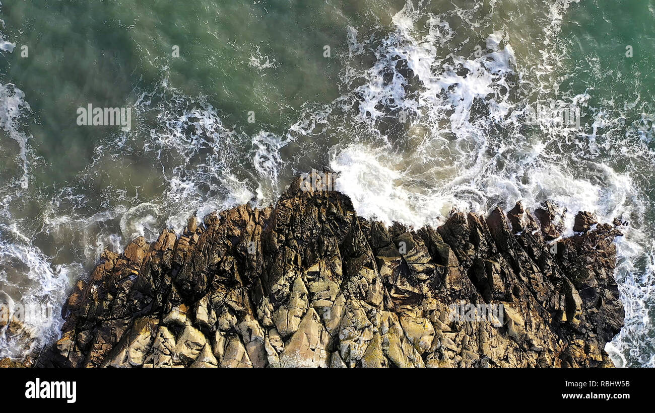 Aerial overhead view of beautiful breaking ocean waves against a rugged ...