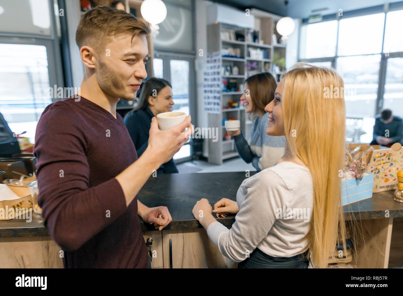 Young smiling and talking barista working at coffee shop behind the bar ...