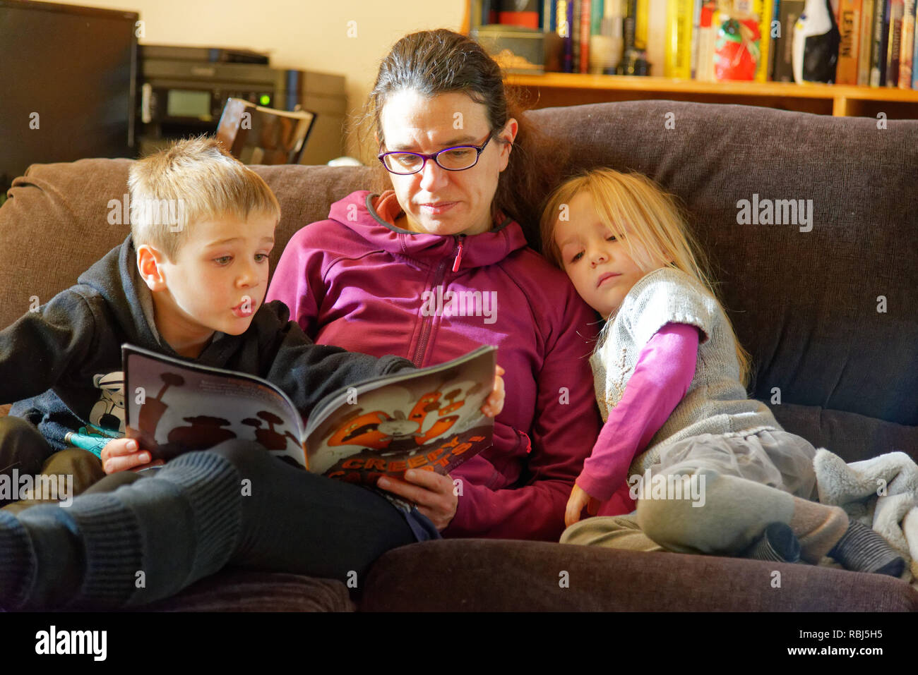 A mum sat on a sofa reading a book to her two young children Stock ...