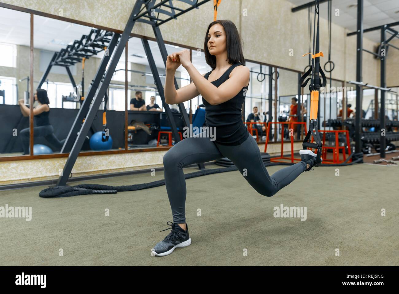 Young fitness woman doing exercises using the straps system in the gym ...