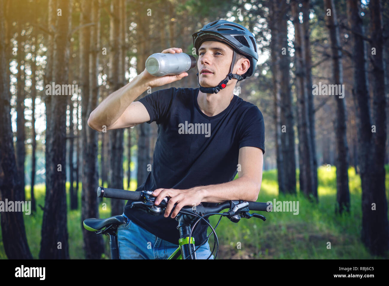 A cyclist in a helmet drinking water from a bottle while riding in the ...
