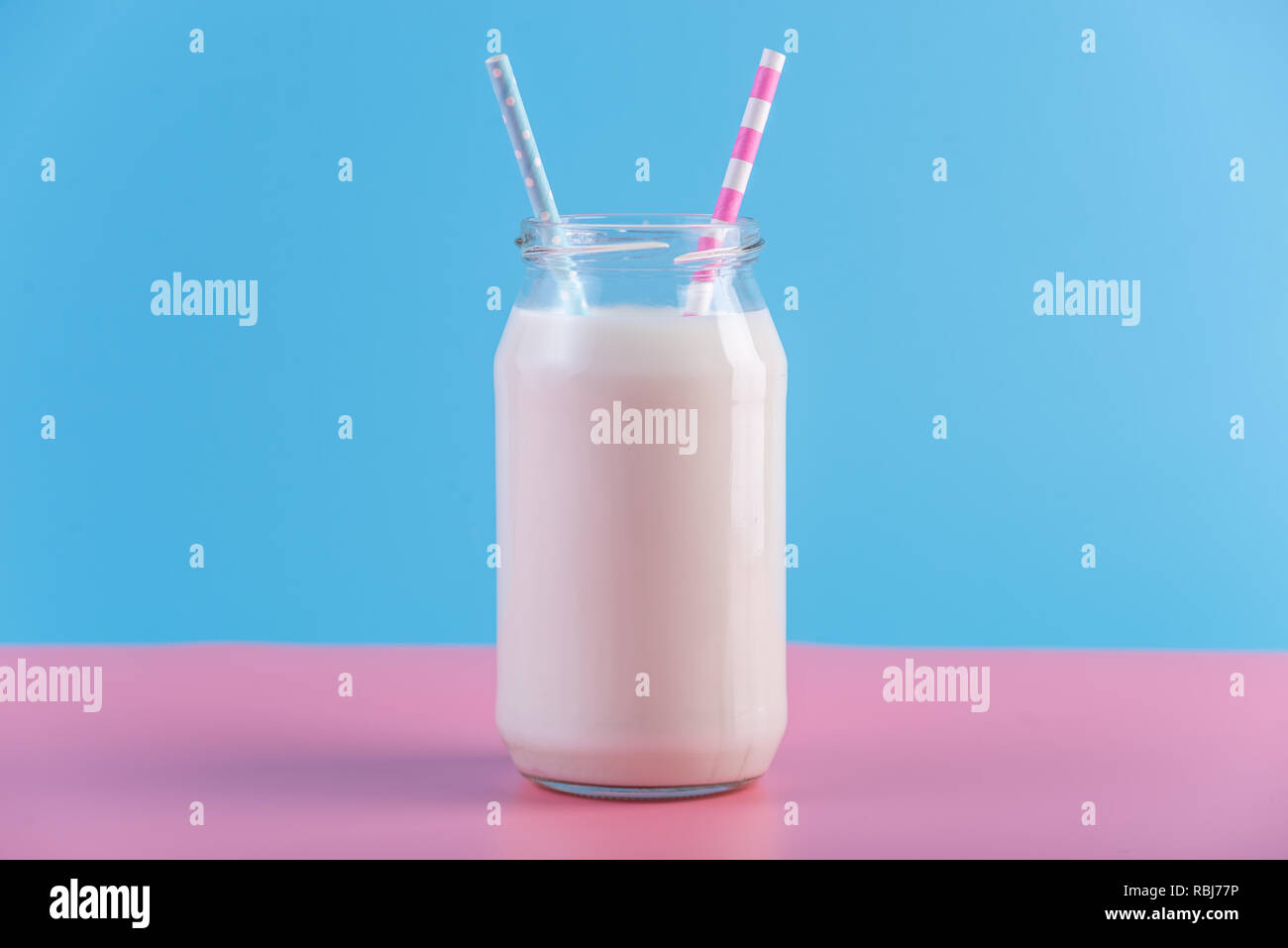 Glass bottle of fresh milk with two straws on pastel background ...