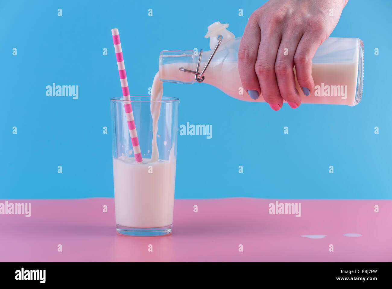 A woman's hand pours fresh milk from a glass bottle into a glass on a ...